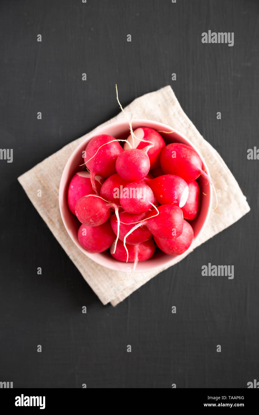 Fresh red radishes in a pink bowl over black surface, overhead view ...