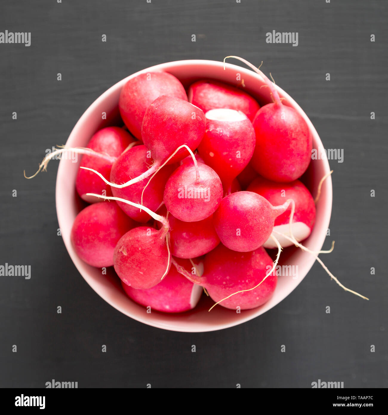 Fresh red radishes in a pink bowl over black background, overhead view ...