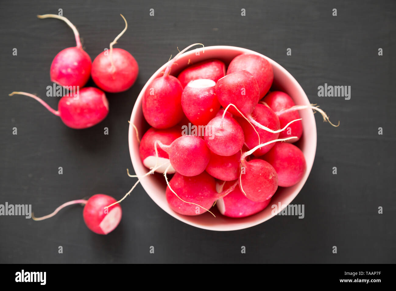 Fresh red radishes in a pink bowl over black background, overhead view ...