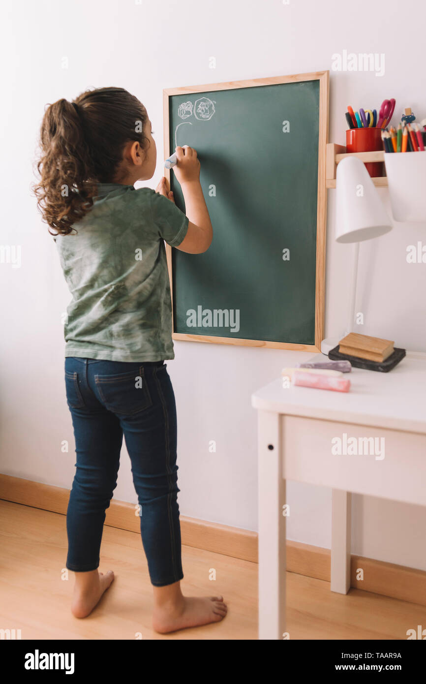vertical photo of a little girl drawing with a chalk on the chalkboard ...
