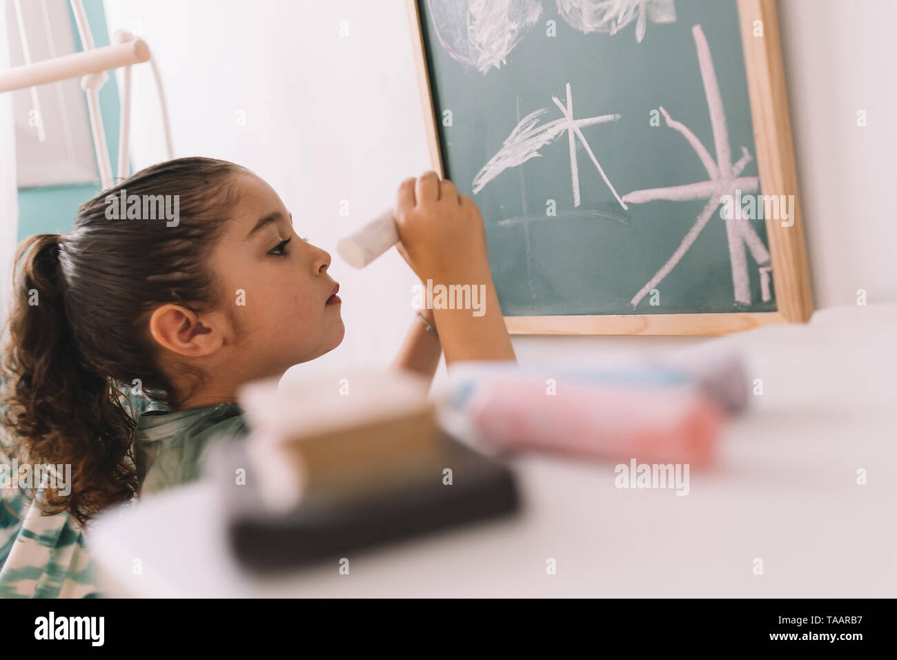 little girl concentrated drawing with a chalk on the blackboard at her ...