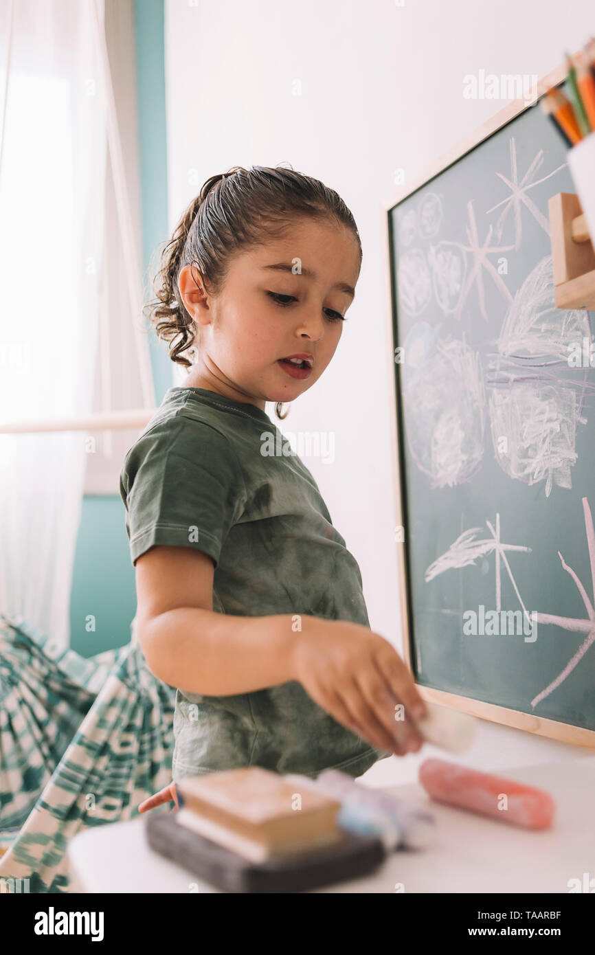 little girl picking up a chalk to draw on the blackboard at her room at ...