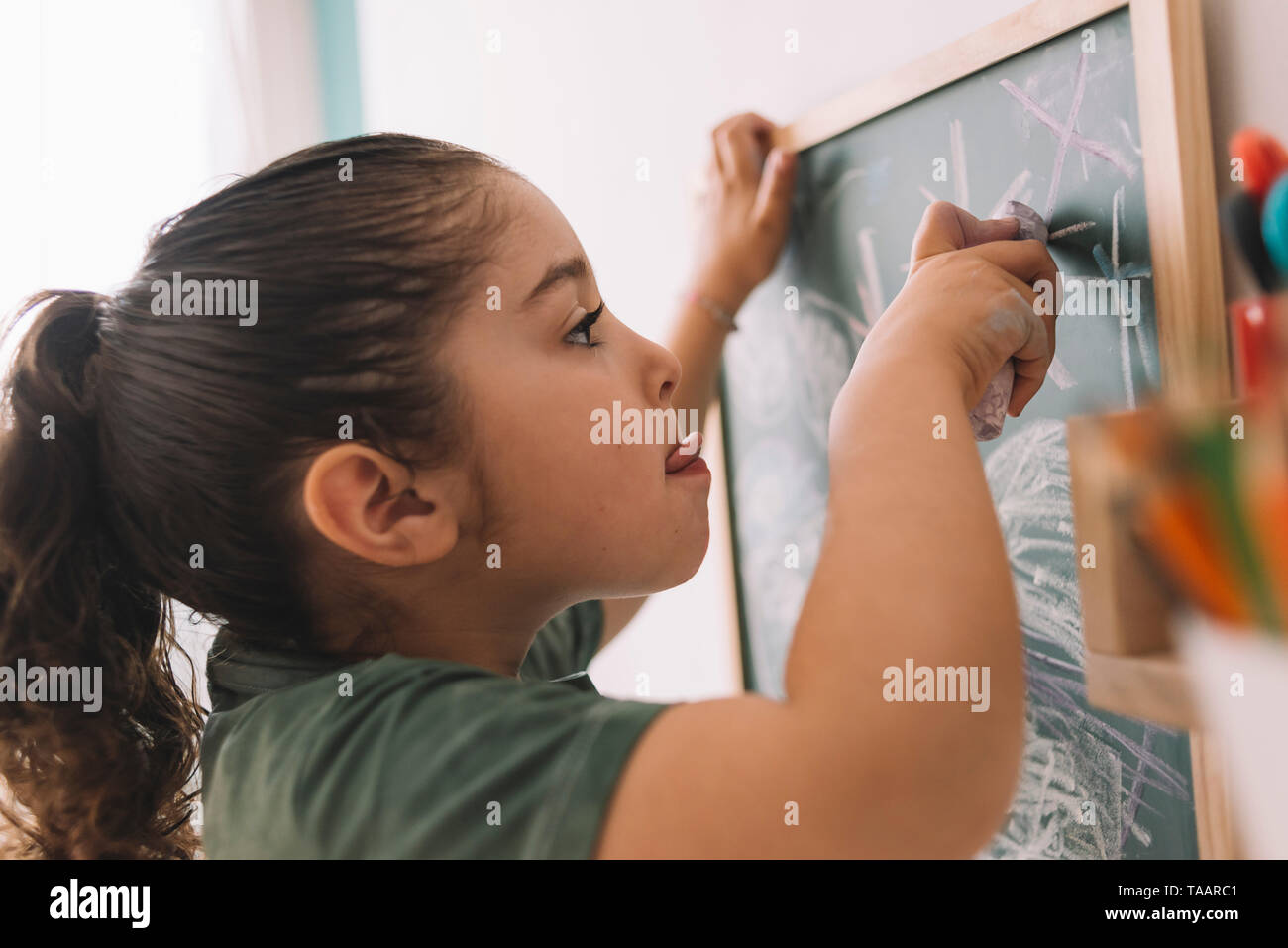 little girl focused drawing with a chalk on the blackboard at her room ...