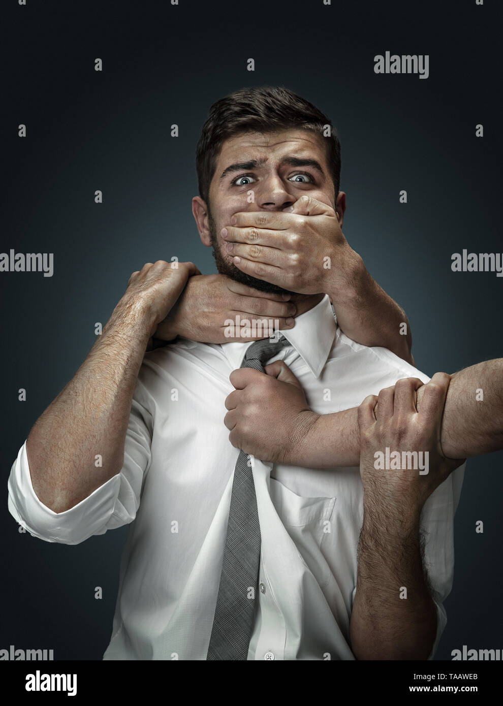 A scared male model on dark background. Hands behind the scene don't ...