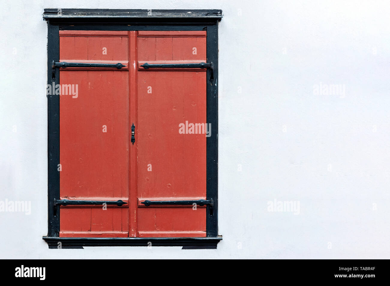 The rectangular window is covered with wooden shutters in red against ...