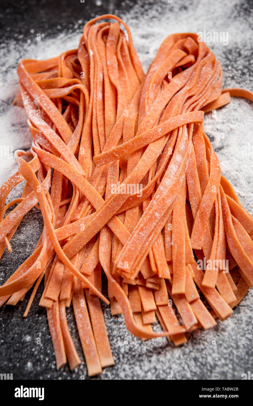 Red homemade raw tagliatelle pasta. Dark marble background with flour ...