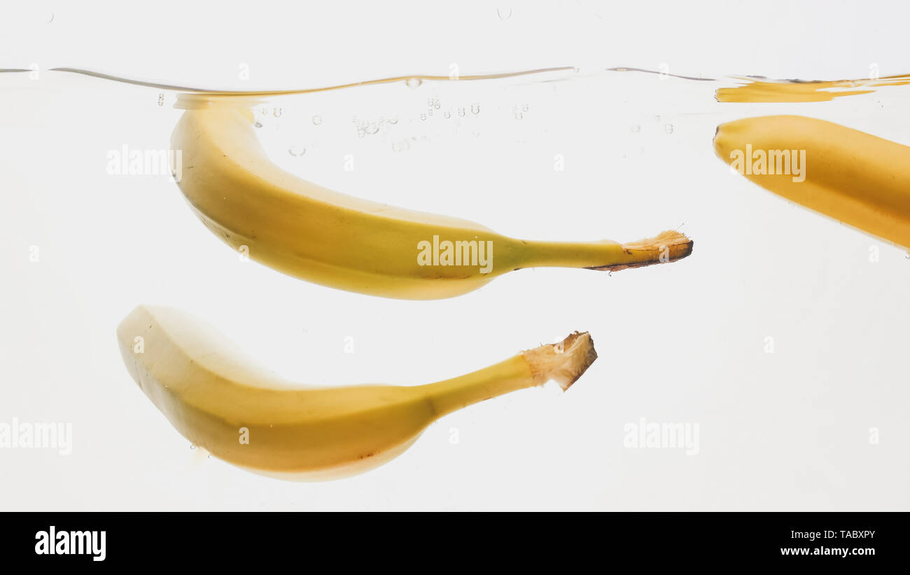 Closeup image of fresh ripe bananas falling and splashing in water ...