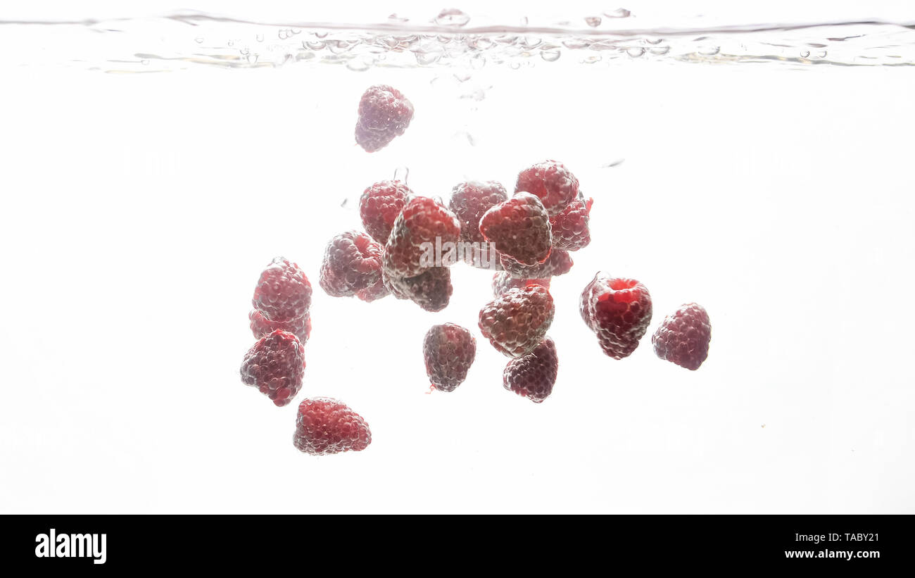 Closeup image of lots of fresh ripe raspberries falling and splashing ...