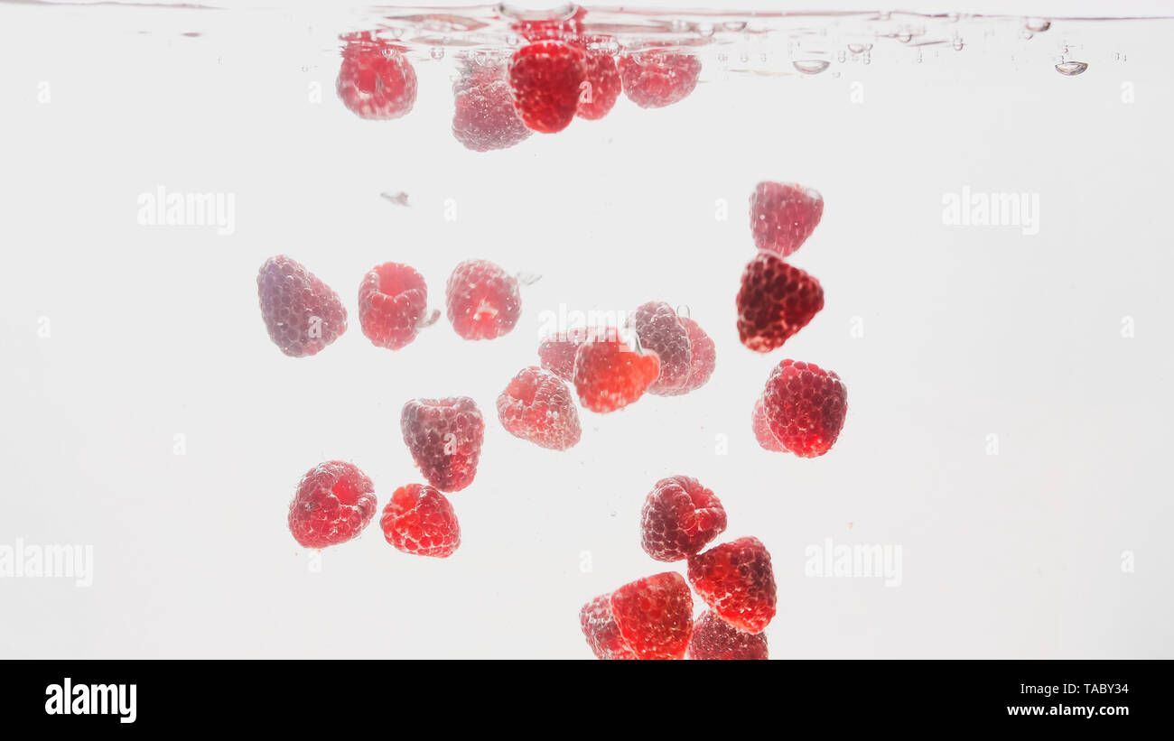 Closeup image of lots of fresh ripe raspberries falling and splashing ...