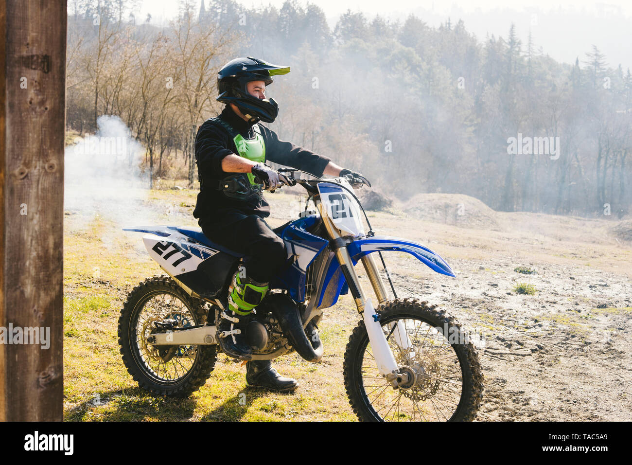 Motocross driver on motorbike with smoke coming out of exhaust pipe ...