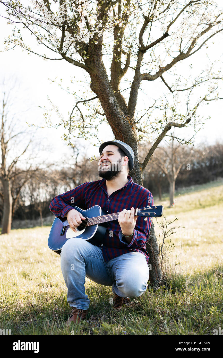 Man playing guitar at a tree on a meadow Stock Photo - Alamy
