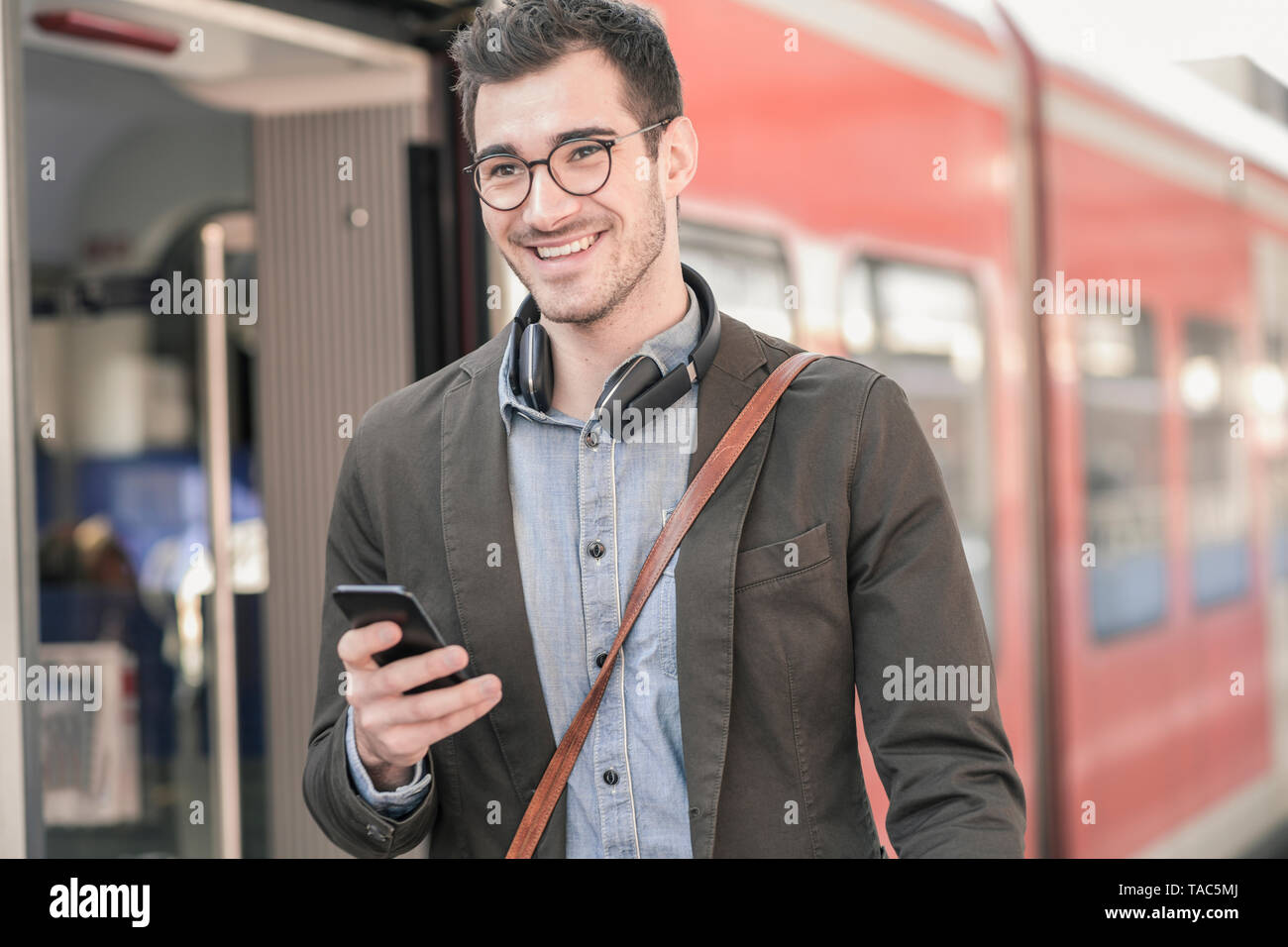 Smiling young man with cell phone at commuter train Stock Photo - Alamy