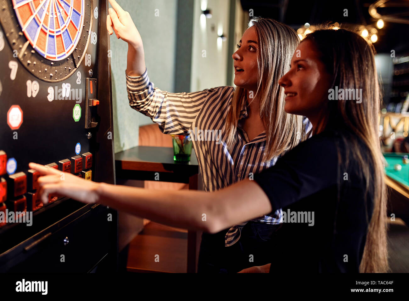 Two women playing darts setting electronic dartboard Stock Photo - Alamy