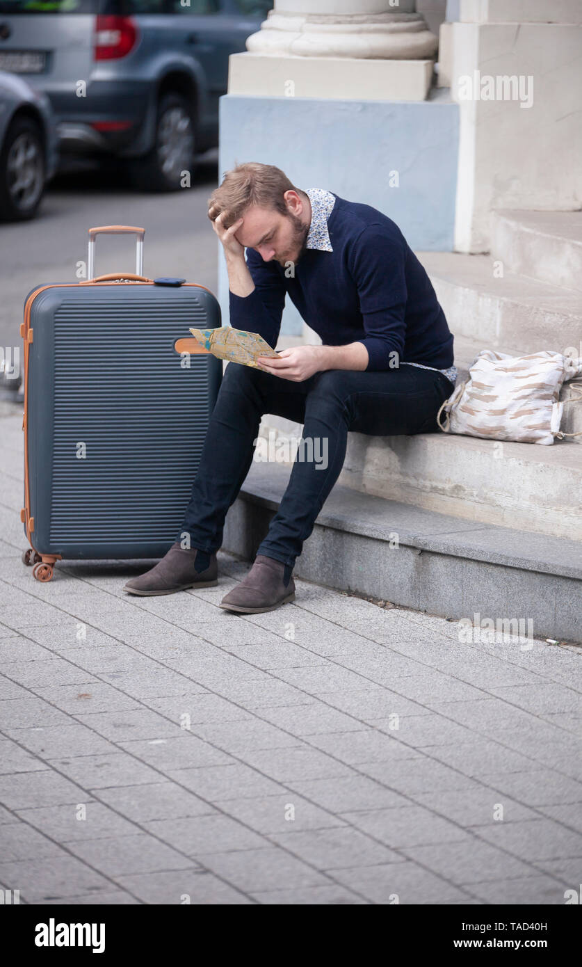 one young man, traveler or tourist, feeling lost on a street, sitting ...