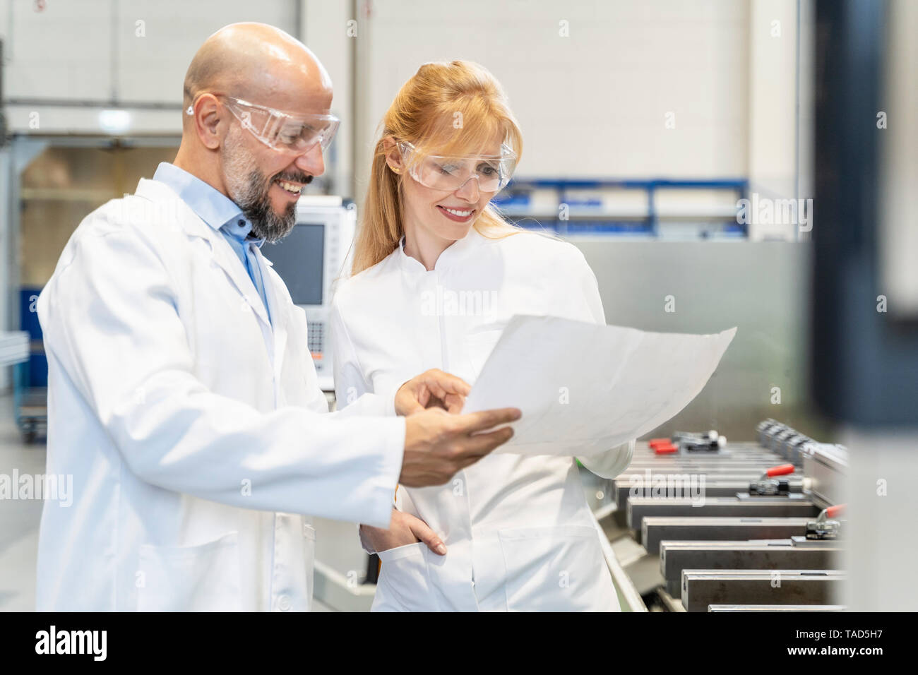 Two happy technicians wearing lab coats and safety glasses looking at ...