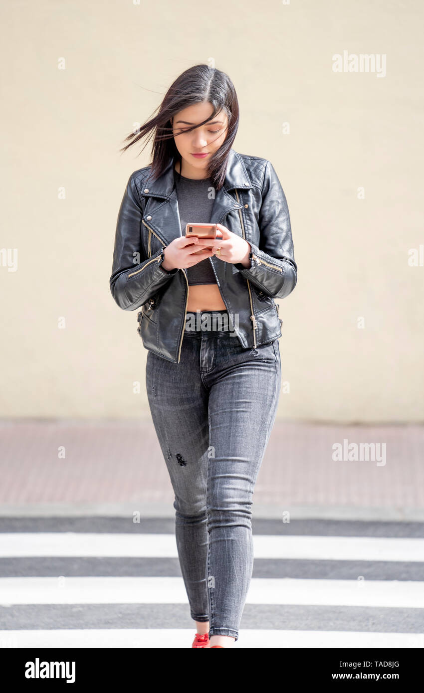 Young woman crossing the pedestrian crossing and using mobile phone ...