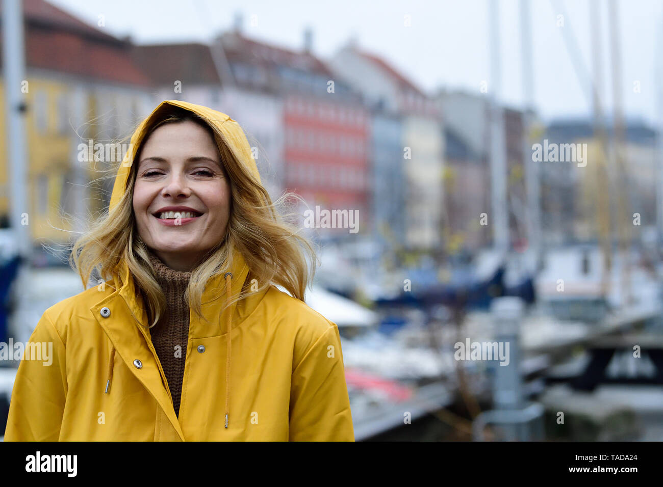 Denmark, Copenhagen, portrait of happy woman at city harbour in rainy ...