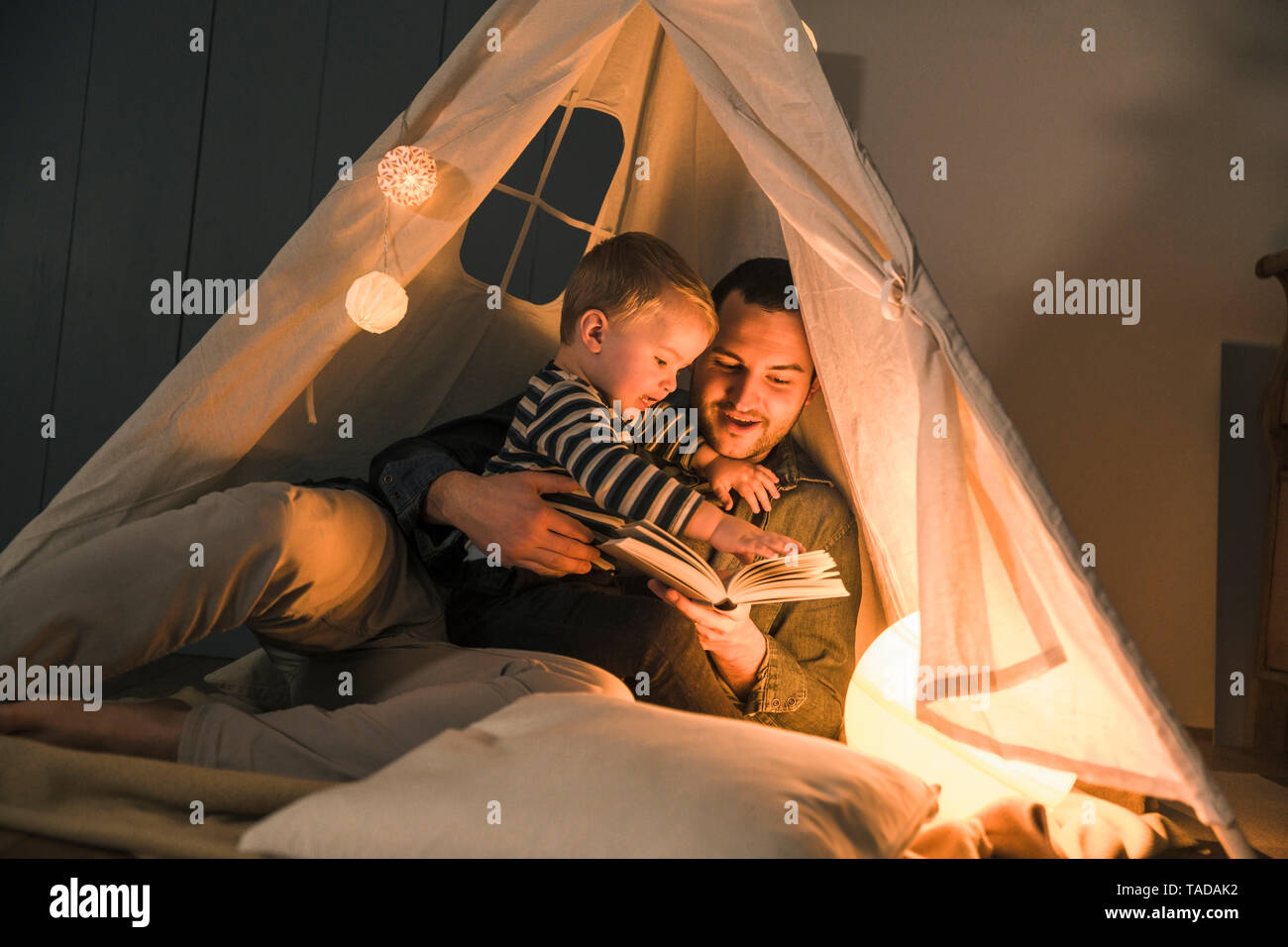 Father reading book to son at an illuminated tent at home Stock Photo ...