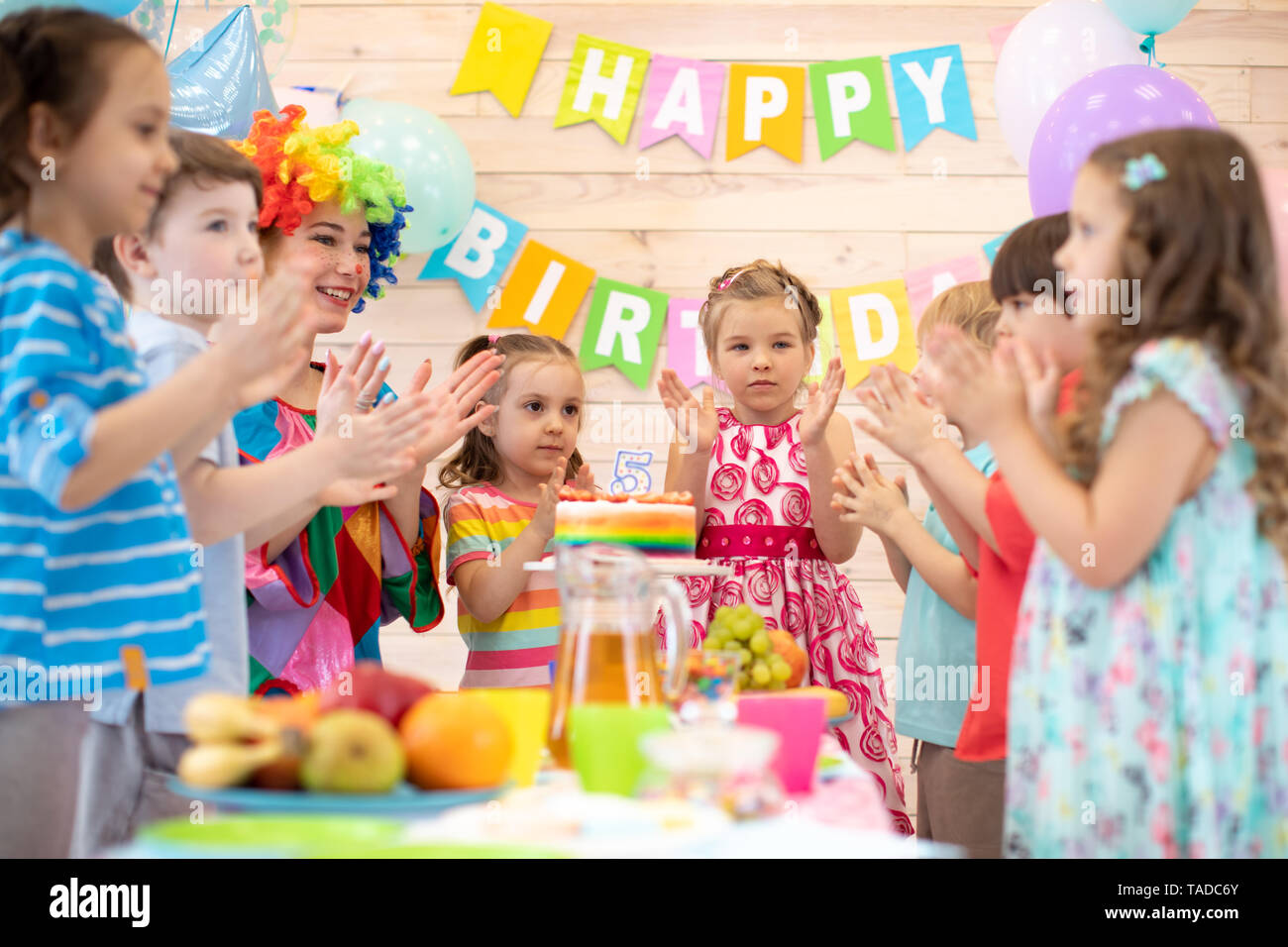 Children group with clown clown clap around table with birthday cake ...