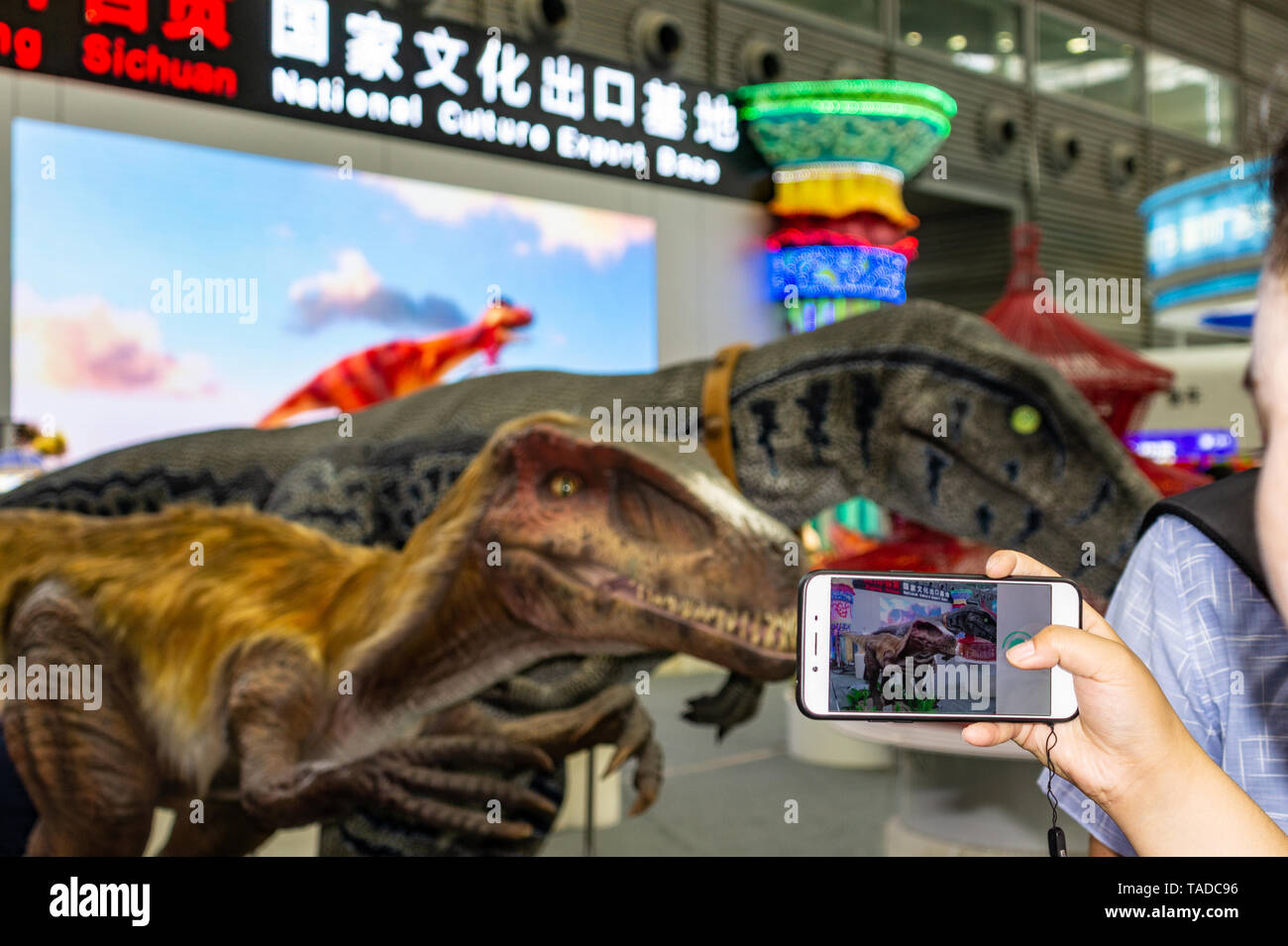 Screen of mobile phone shows animatronic dinosaurs as person, hand ...