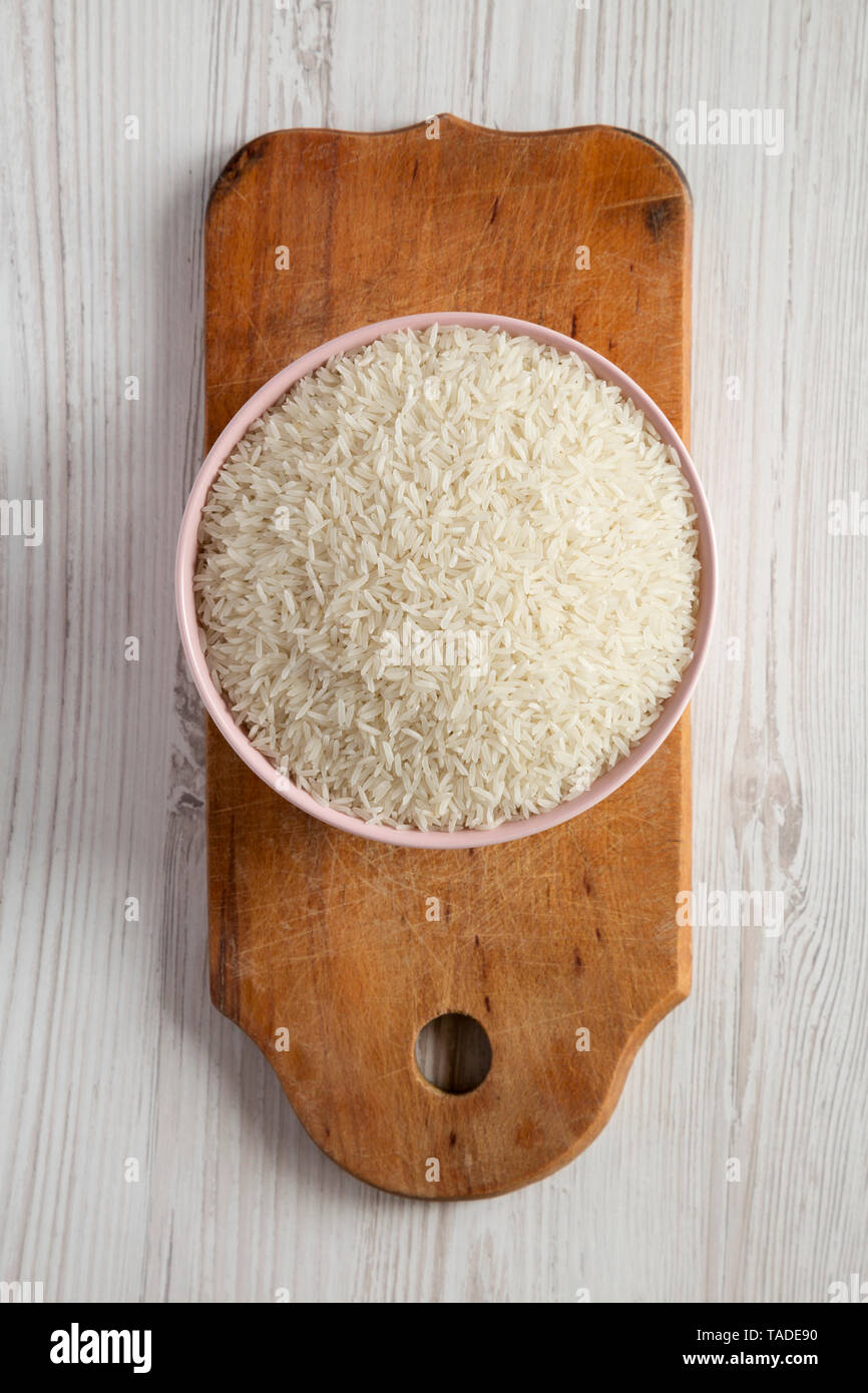 Pink bowl filled with dry white rice basmati on a rustic wooden board ...