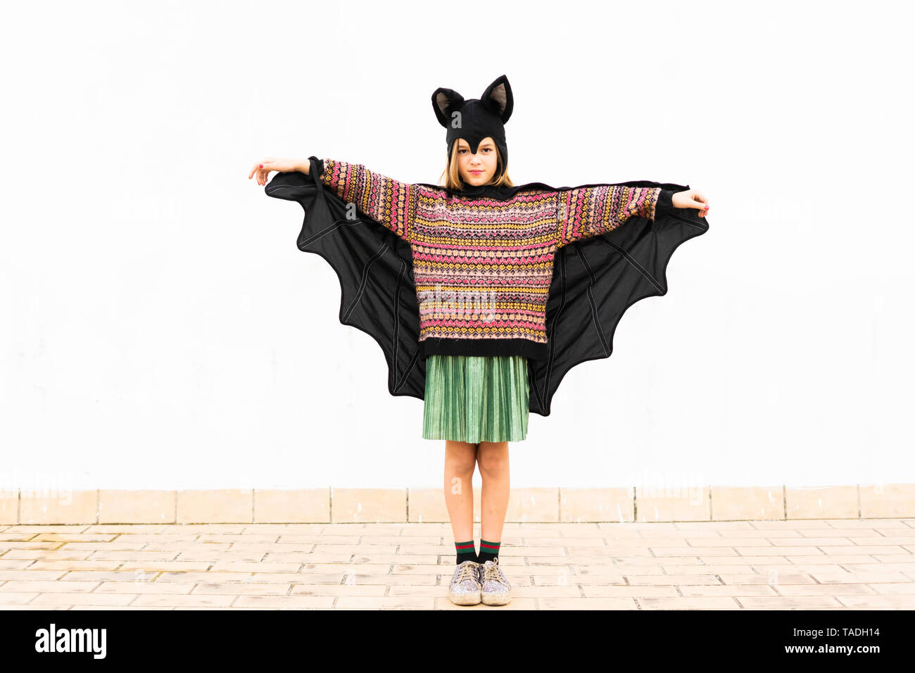 Portrait of girl in bat costume spreading wings in front of white wall ...