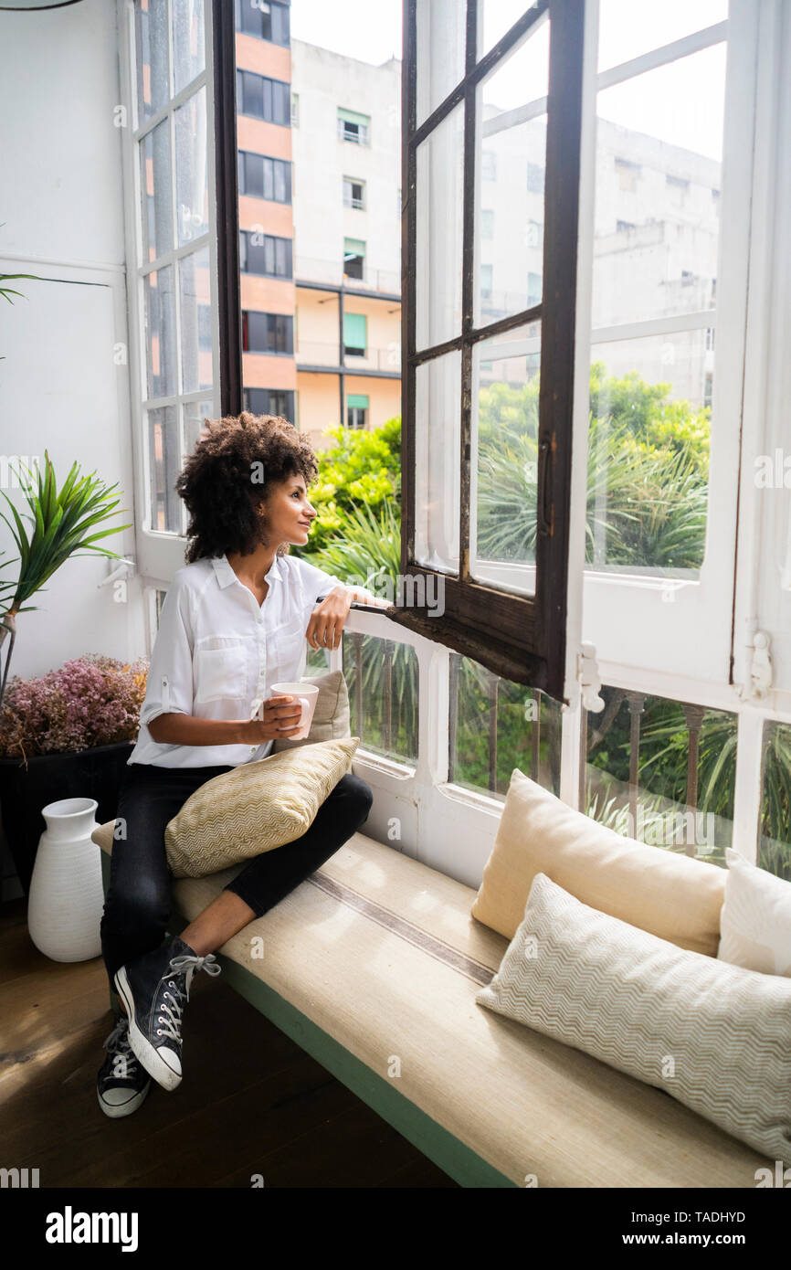 Beautiful woman sitting on bench, looking out of window, drinking ...