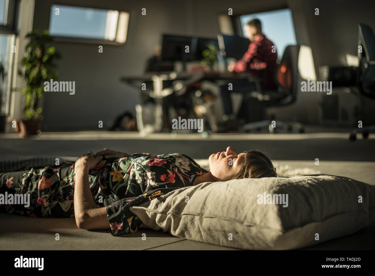 Woman taking a nap, lying on a cushion on the office floor Stock Photo ...