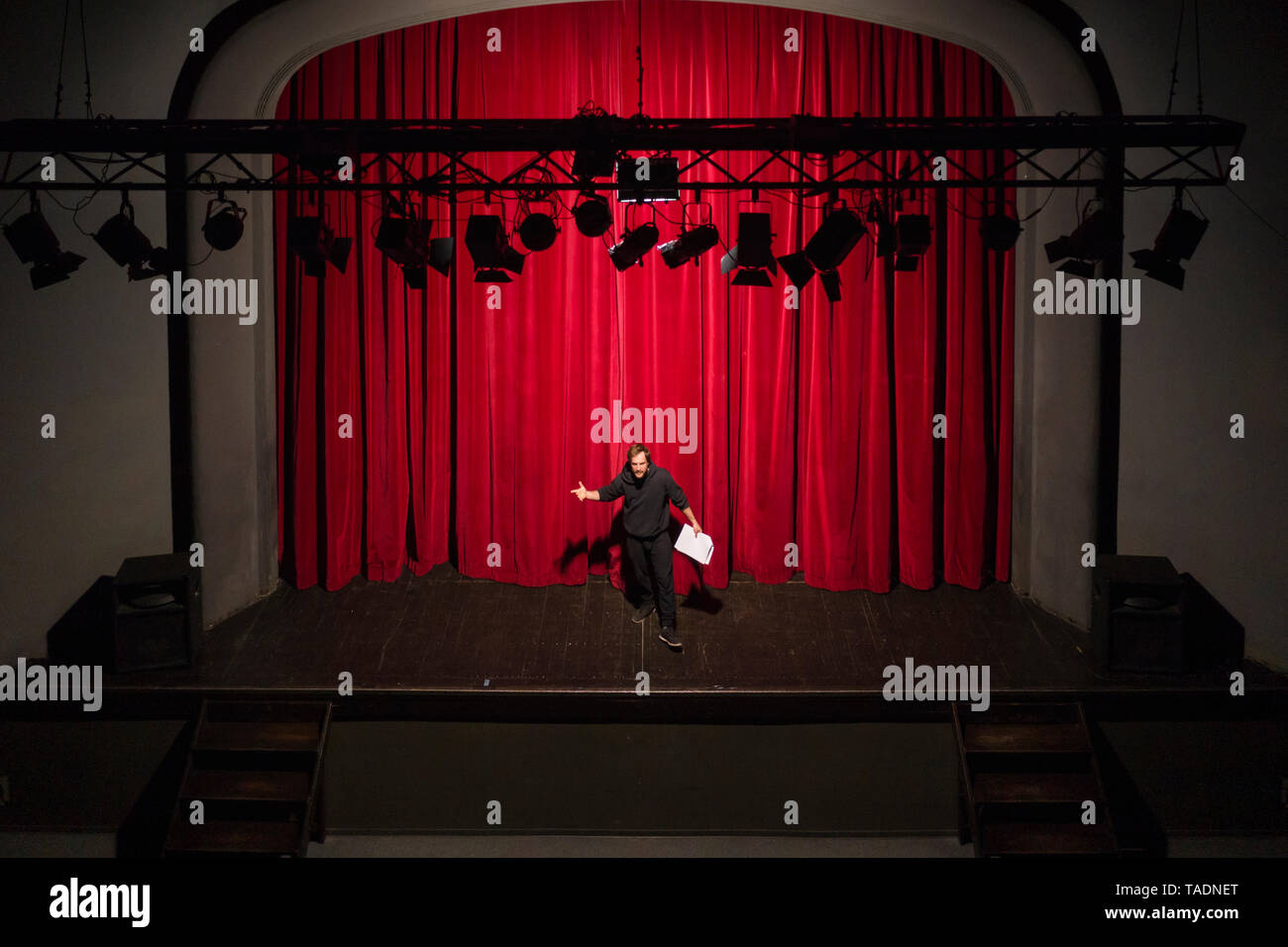 Rehearsing actor with script standing on theatre stage in front of red ...