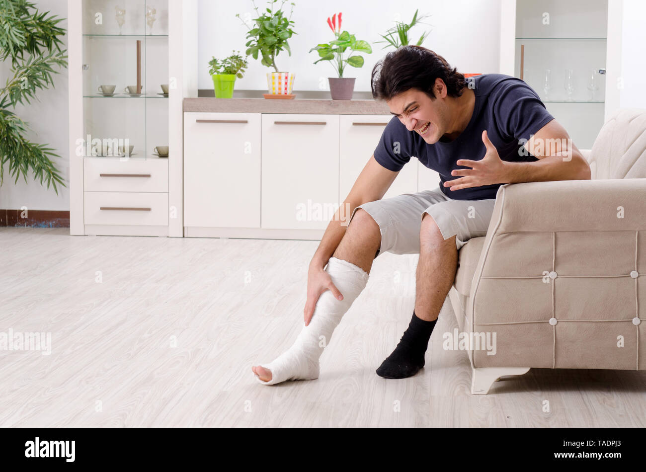 Leg injured young man suffering at home Stock Photo - Alamy
