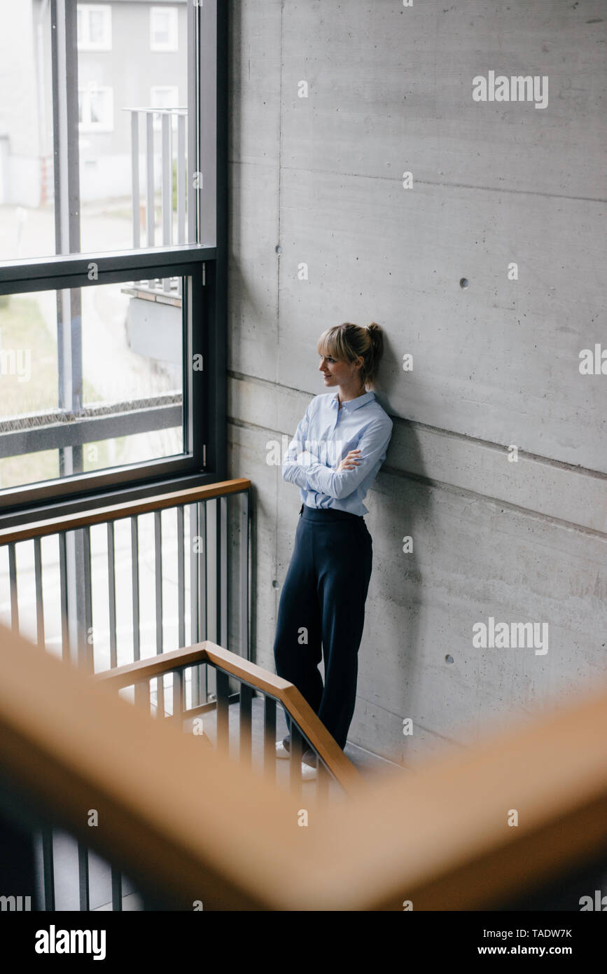 Successful businesswoman leaning on wall, looking out of window, with ...