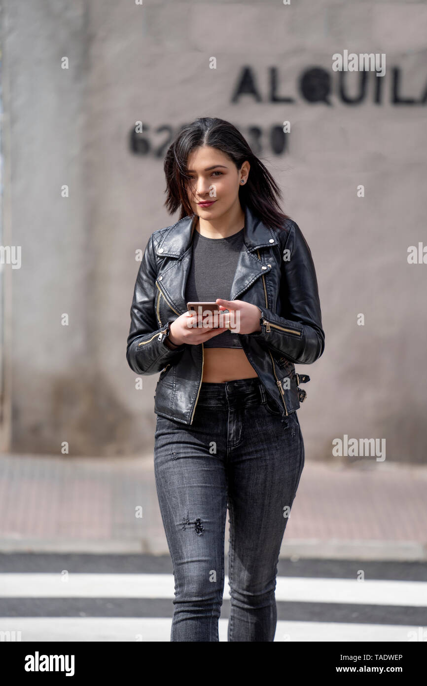 Young woman crossing the pedestrian crossing and using mobile phone ...