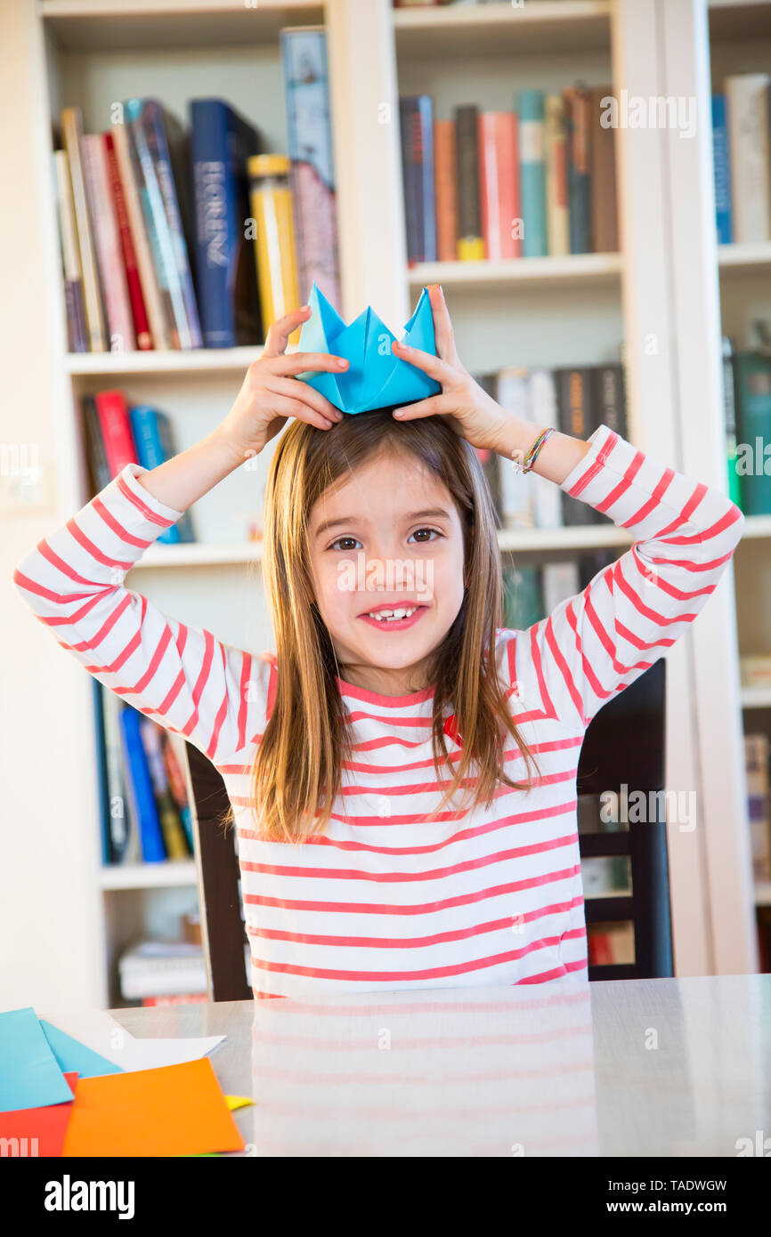 Portrait of smiling girl putting on selfmade paper hat at home Stock ...