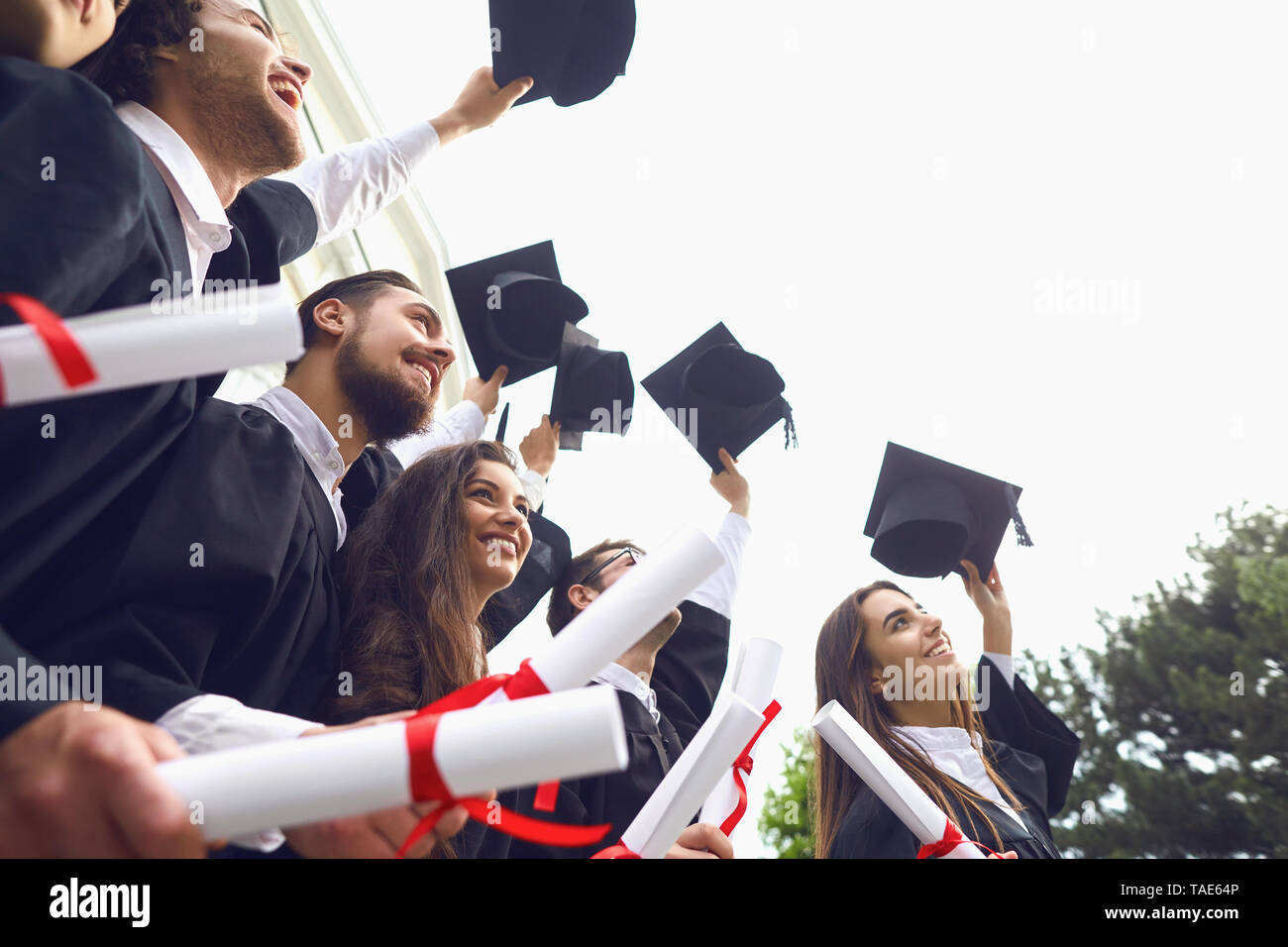 Happy graduates raised their hands with scrolls of diplomas on the ...