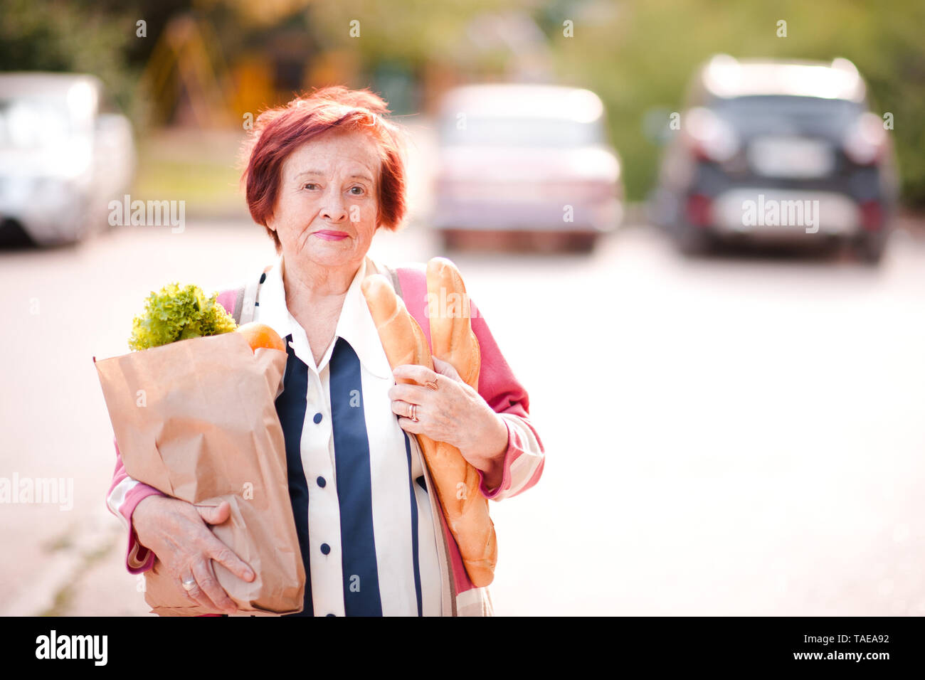 Happy senior woman 70-80 year old holding package of food walking on ...