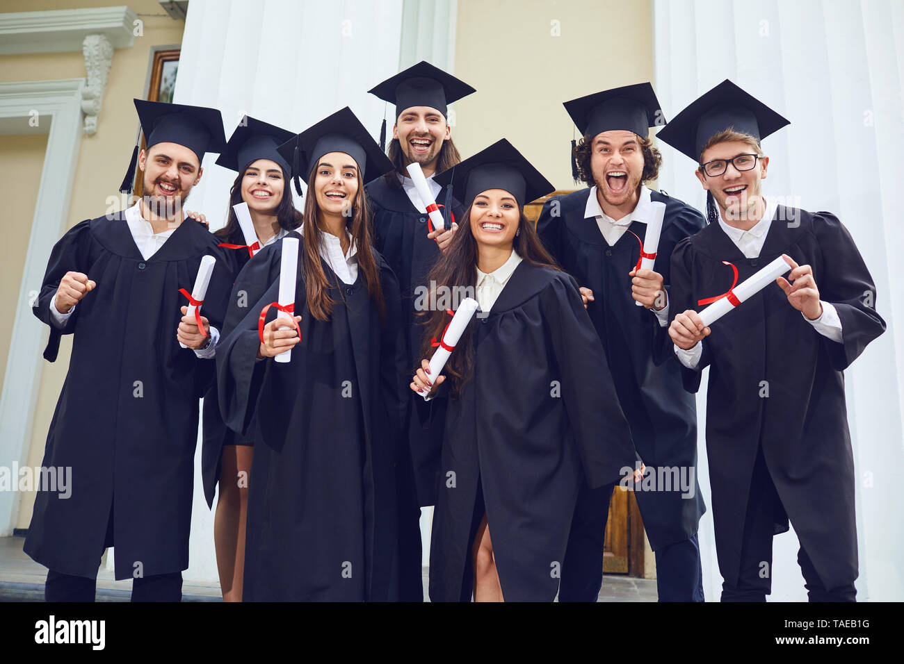 A group of graduates with scrolls in their hands are smiling against ...