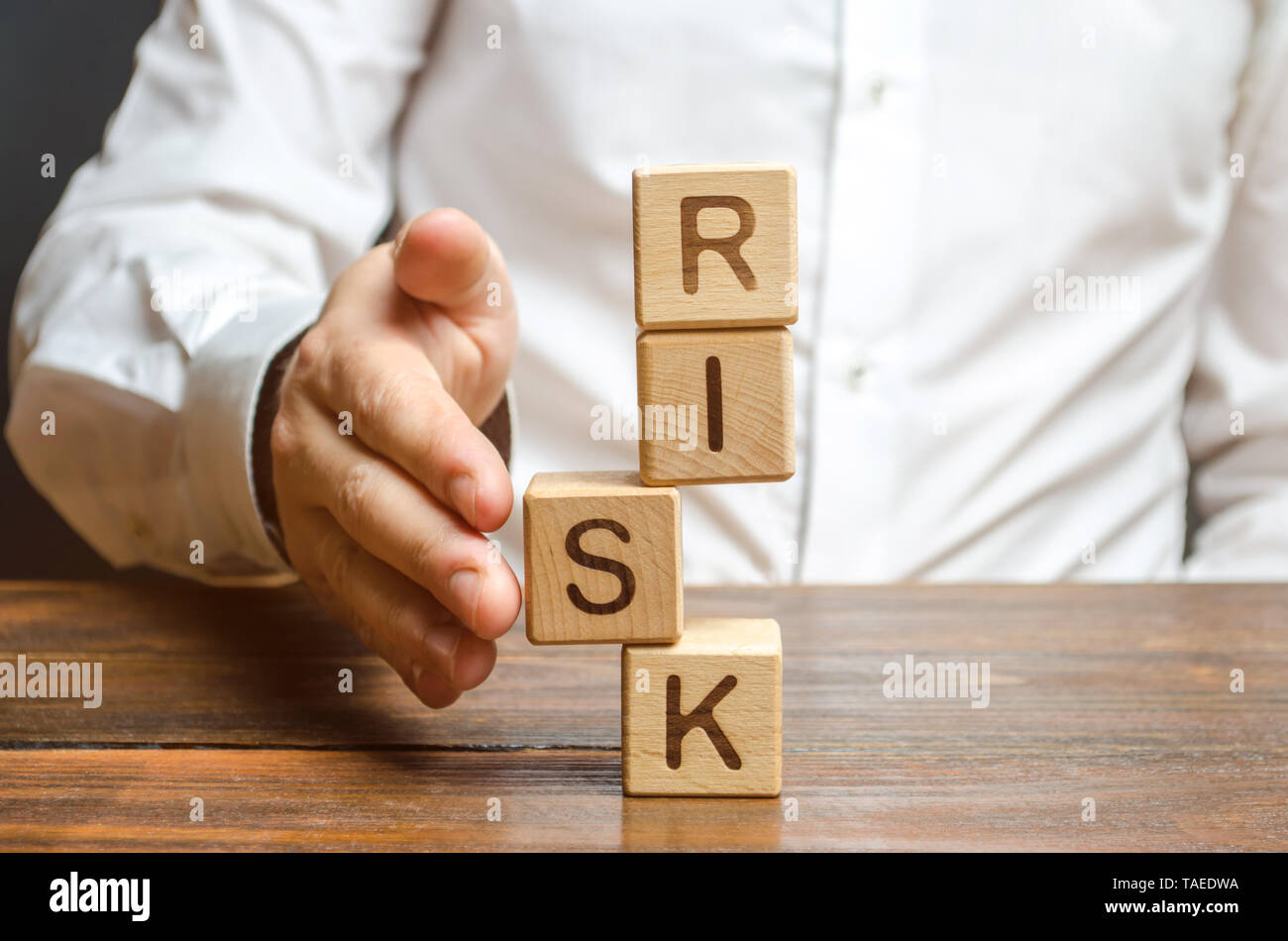 A man straightens a segment in an unstable tower of cubes labeled Risk ...