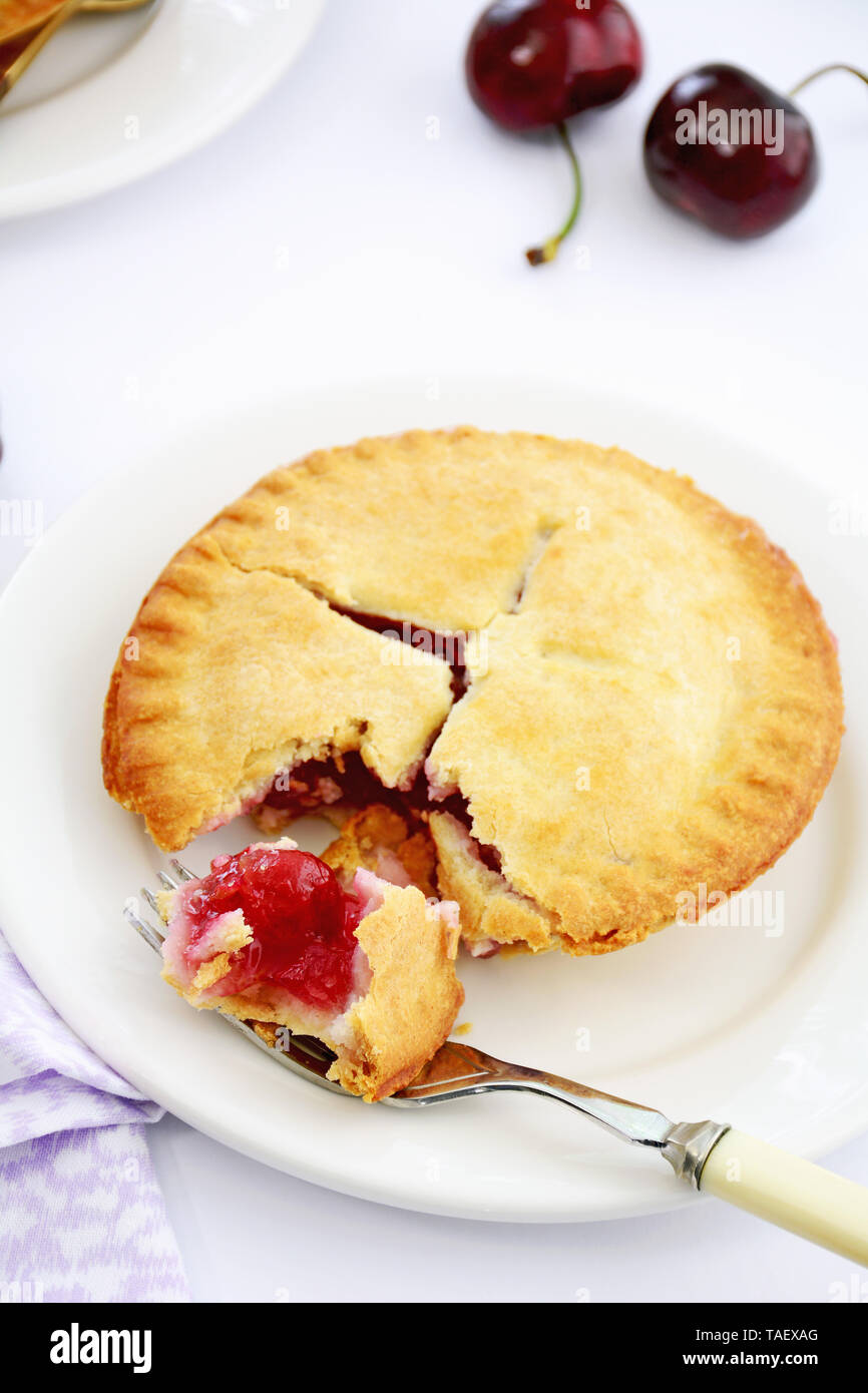 Small individual cherry pie on white plate with vintage fork and fresh ...