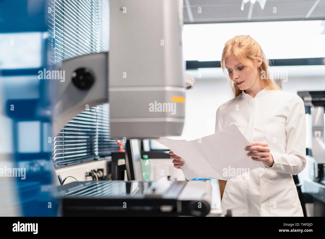 Woman wearing lab coat looking at plan Stock Photo - Alamy