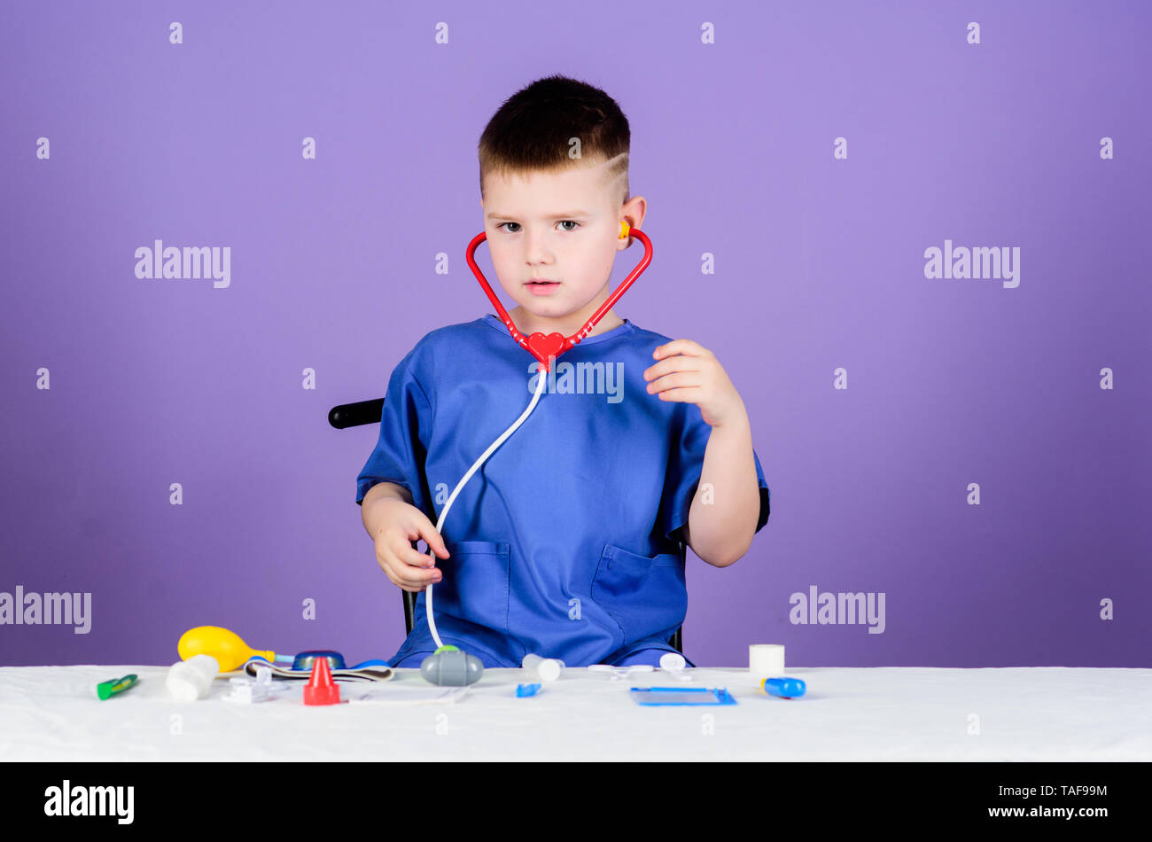 Kid little doctor sit table with stethoscope and medical tools ...