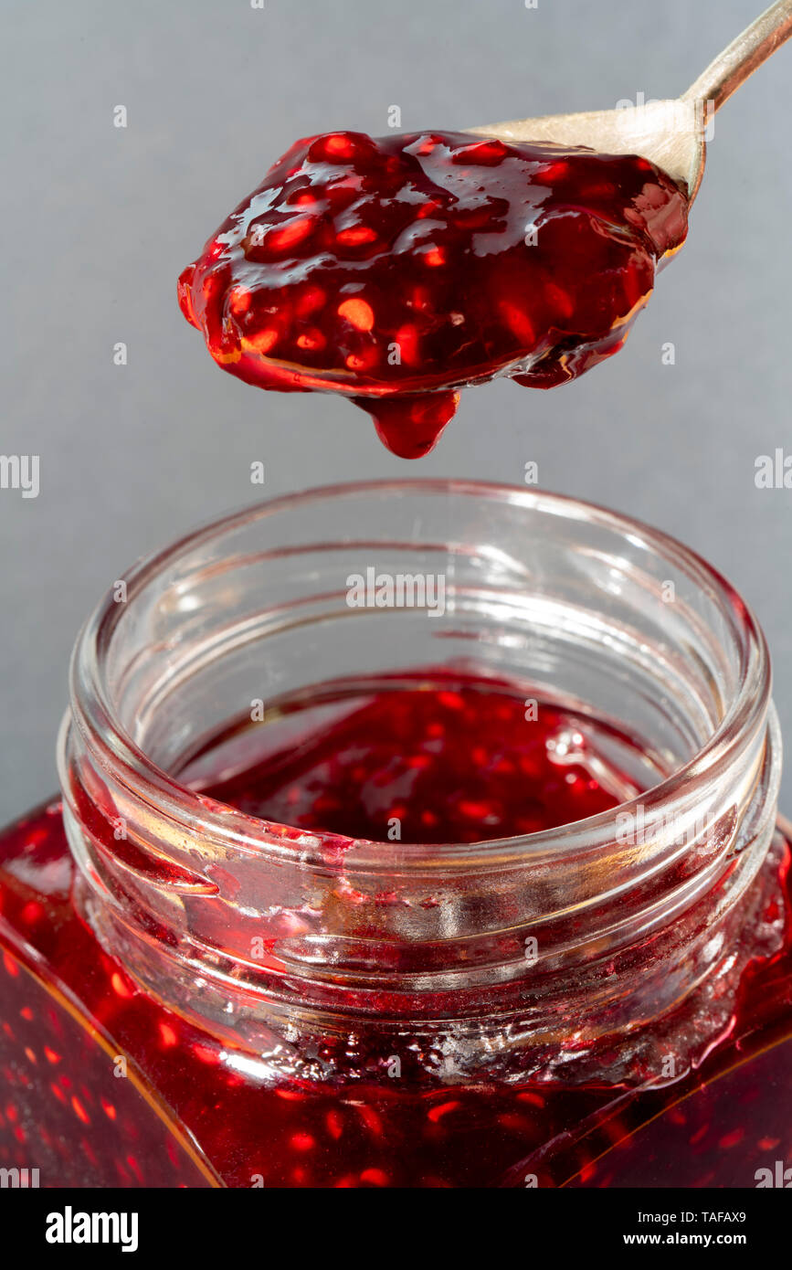 Raspberry jam in a glass jar. Spoon with jam Stock Photo - Alamy
