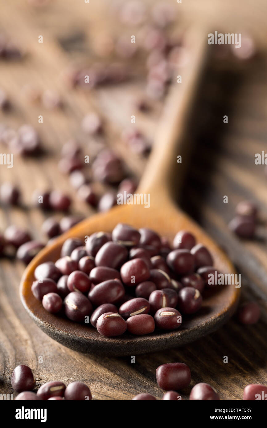 Raw, uncooked, dried adzuki (red mung) beans in wooden spoon on rustic wood table background ...