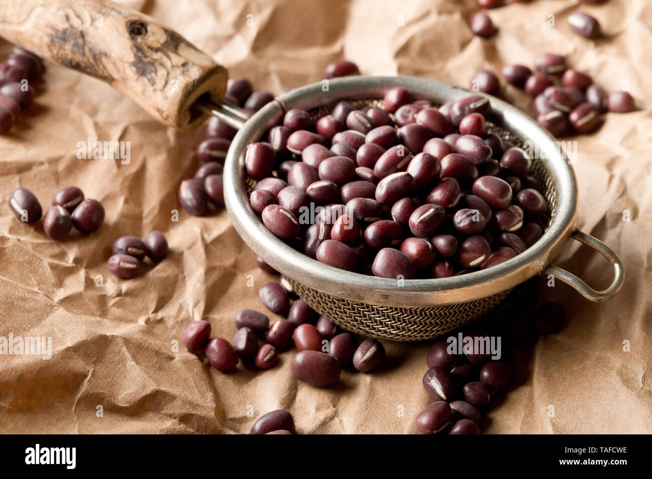 Raw, uncooked, dried adzuki (red mung) beans in small sieve on brown ...