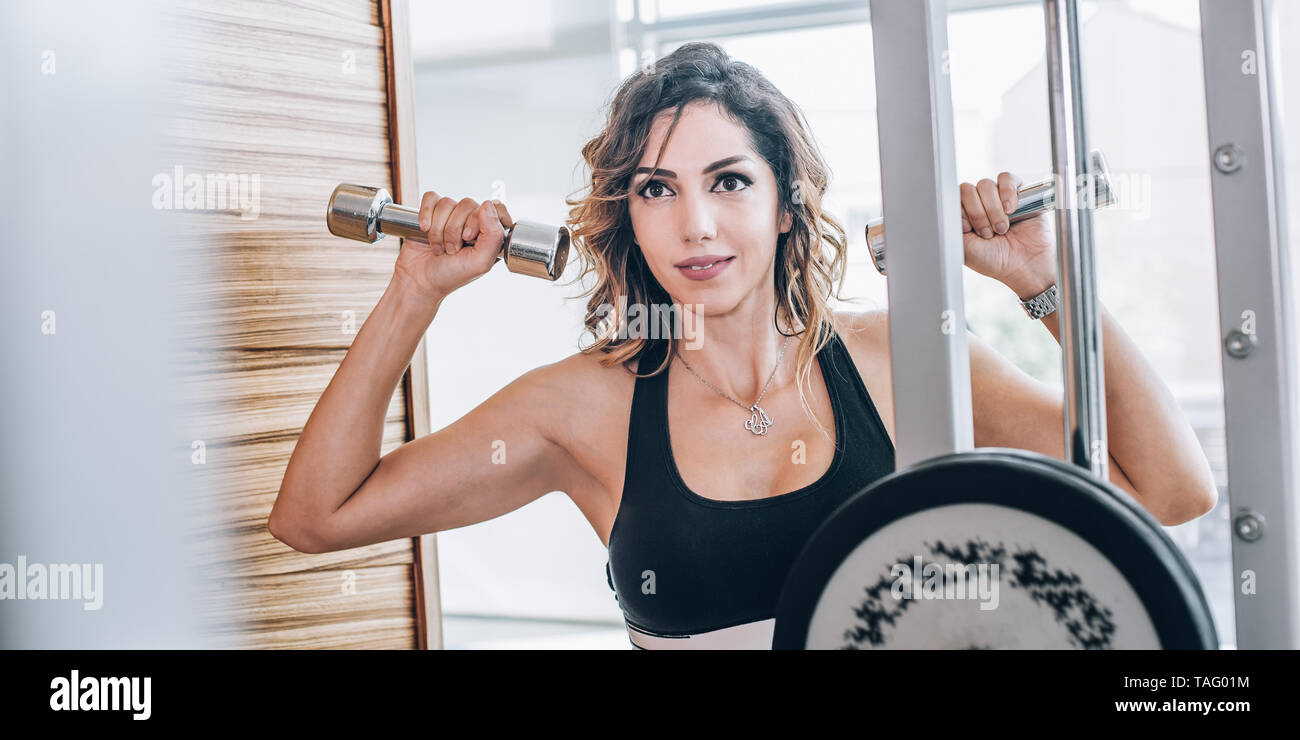 Attractive muscular smiling fitness woman doing exercise with dumbbells ...