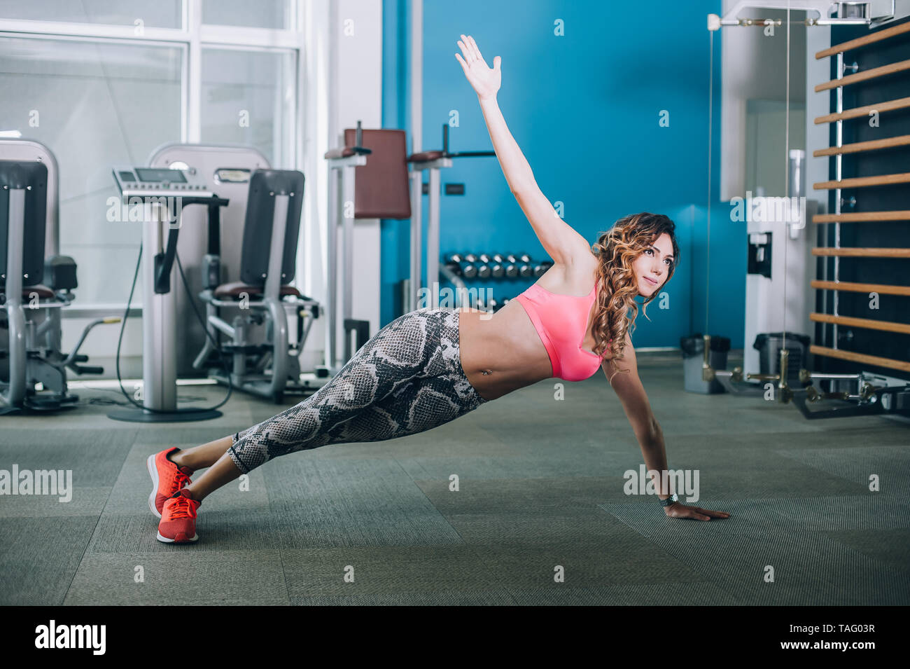 Attractive muscular smiling fitness woman doing hard exercise in modern ...