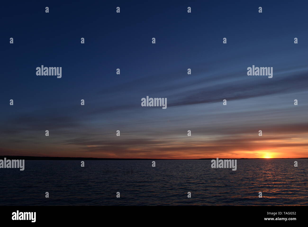 Sunset on the horizon above the water of a lake in a blue sky of ...