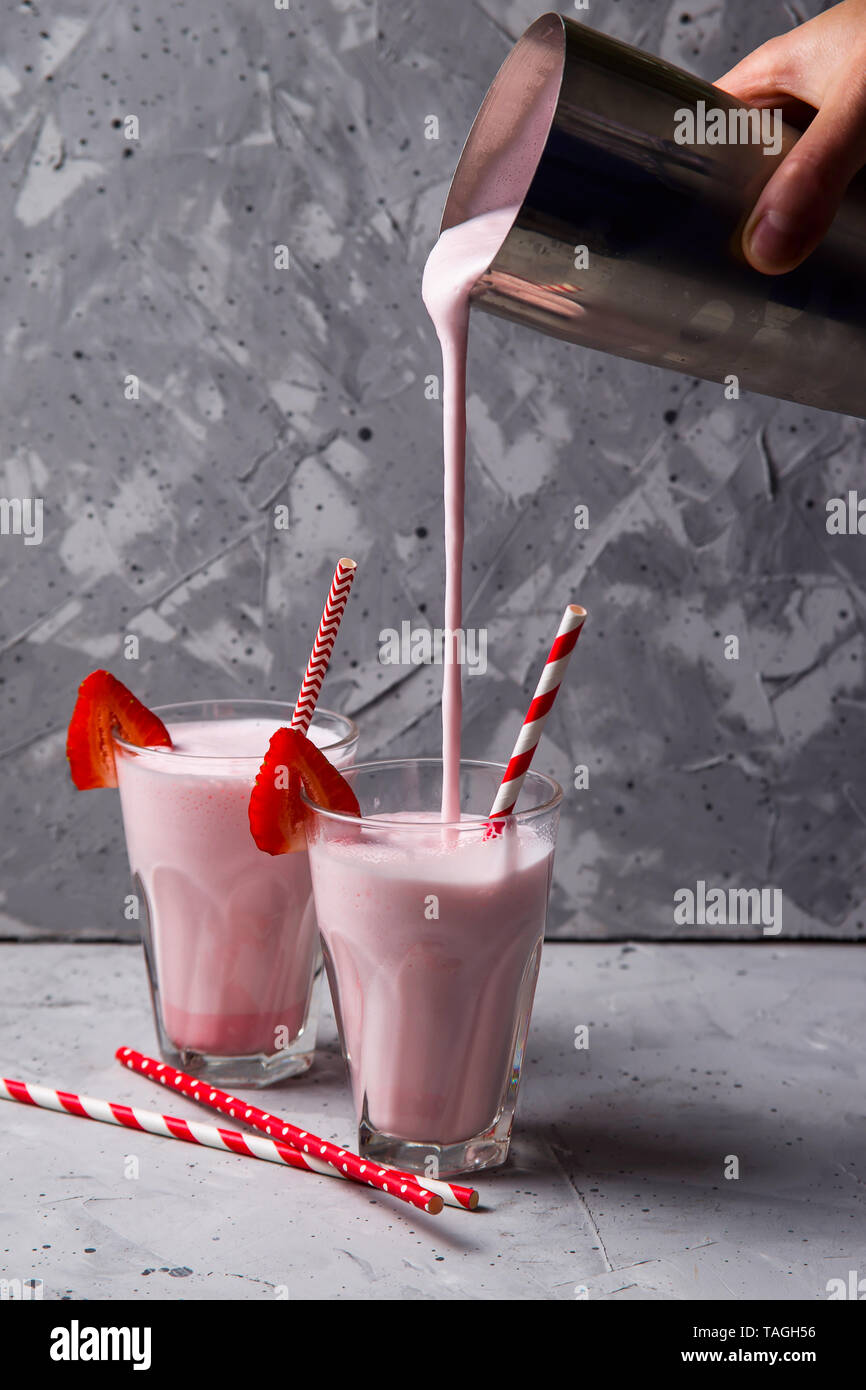 Female hand pours strawberry milkshake from a metal shaker into glass ...