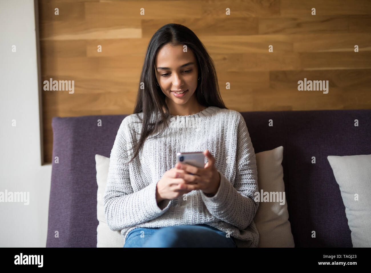 Pretty girl using her smartphone on couch at home in the living room ...
