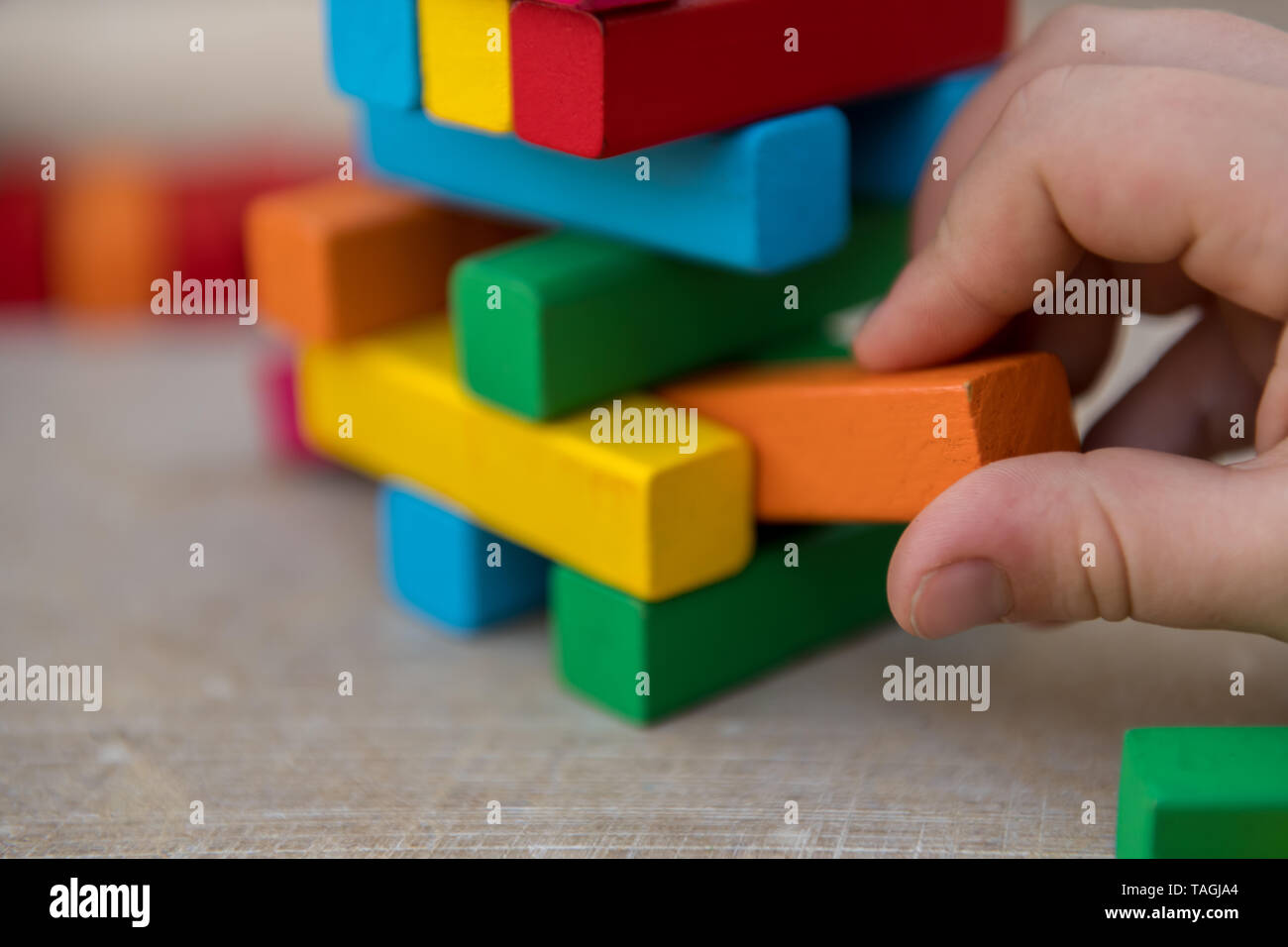 A child removes an orange wooden block from a tower with stacked wooden ...