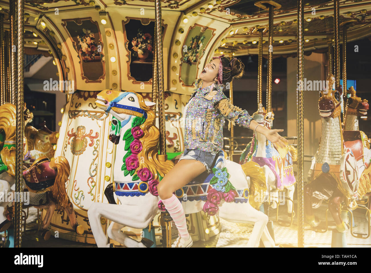 Stylish woman wearing sparkling jacket on the carousel in theme park ...